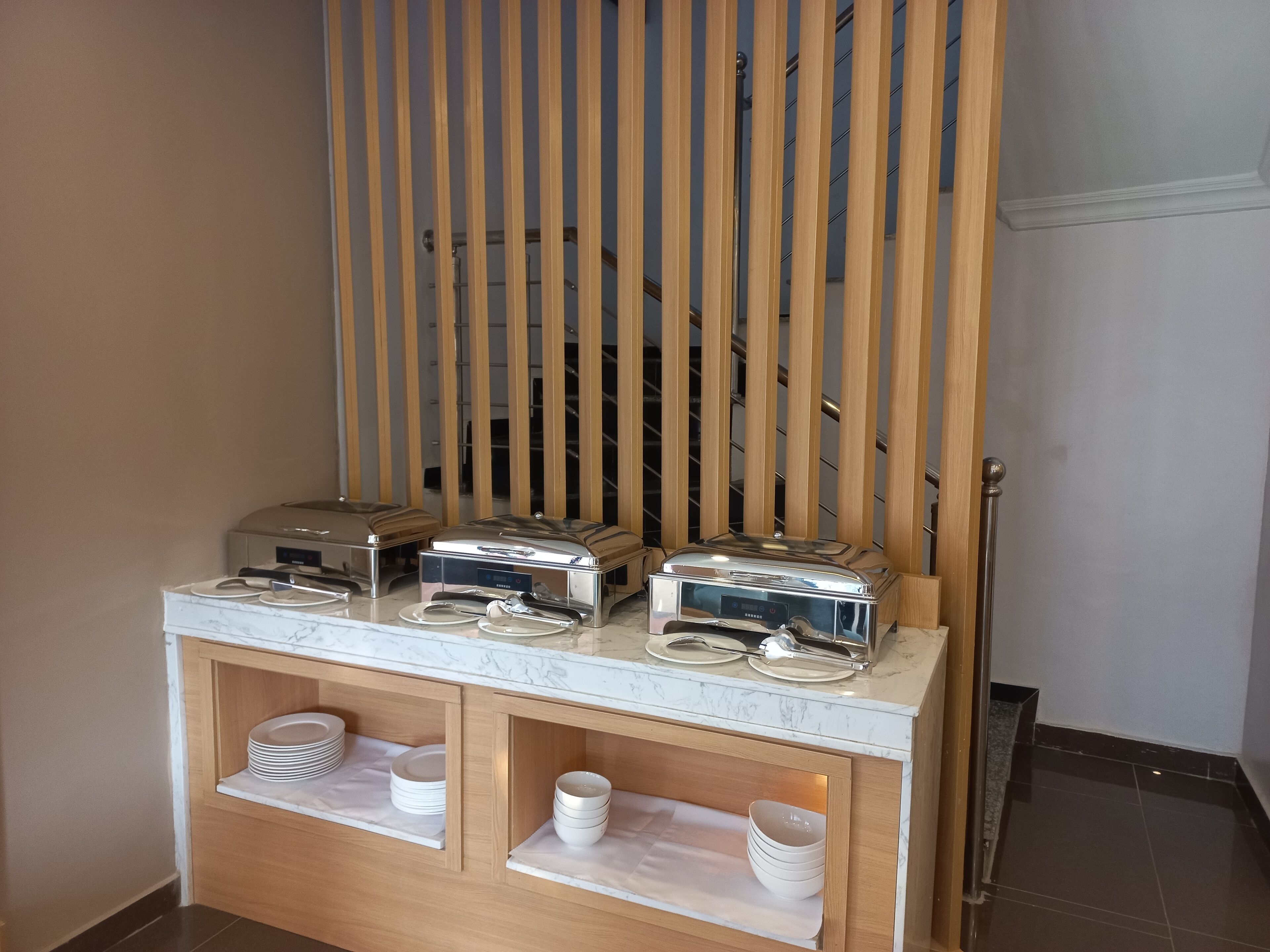 Disposição de buffet com eletrodomésticos de aço inoxidável e pratos brancos em bancadas de mármore.