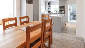 Uma cozinha moderna com armários cinzentos, uma mesa de jantar de madeira e uma ilha embutida com uma pia.