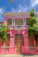 Um edifício rosa com varanda, janelas amplas e um portão.