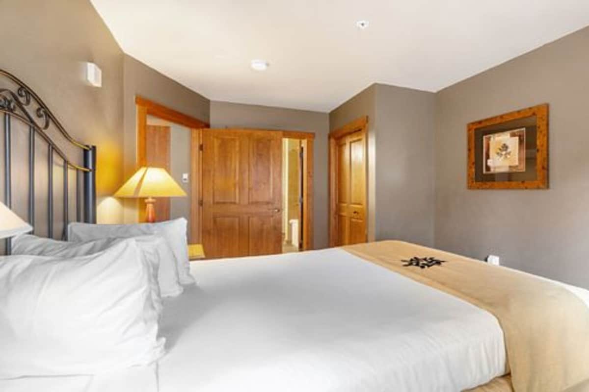 Quarto de hotel com uma cama, uma escrivaninha, uma luminária e um quadro na parede.