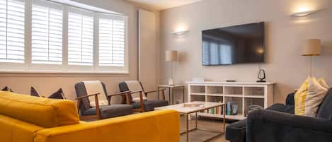 Uma sala de estar com sofá, cadeiras, mesa de centro, televisão e estante de livros.
