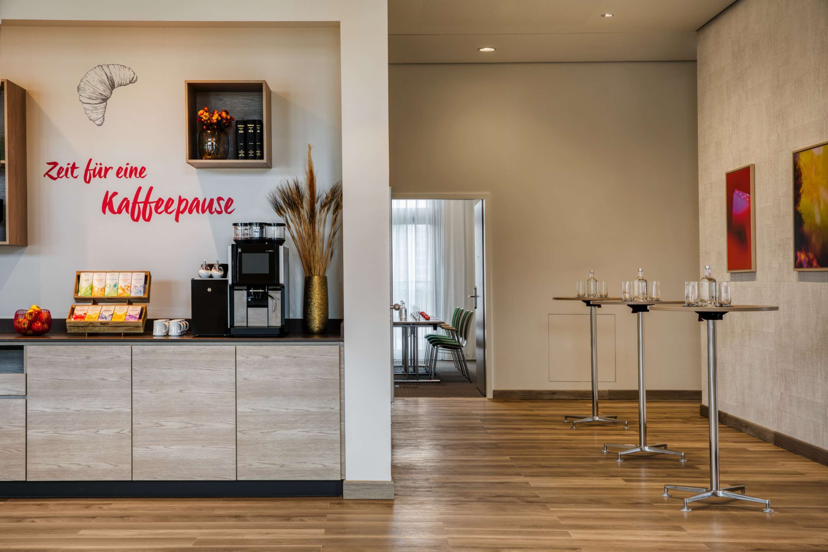 Um lobby moderno de hotel com um espaço para café, área de refeições e balcão de recepção.