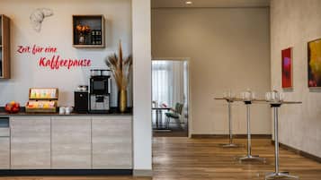 Um lobby moderno de hotel com um espaço para café, área de refeições e balcão de recepção.