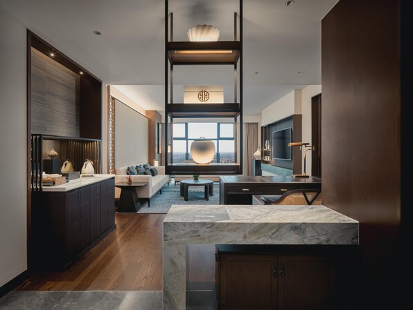 Quarto de hotel moderno com ilha de cozinha em mármore, sofá, mesa de jantar e uma janela grande com vista para a cidade.