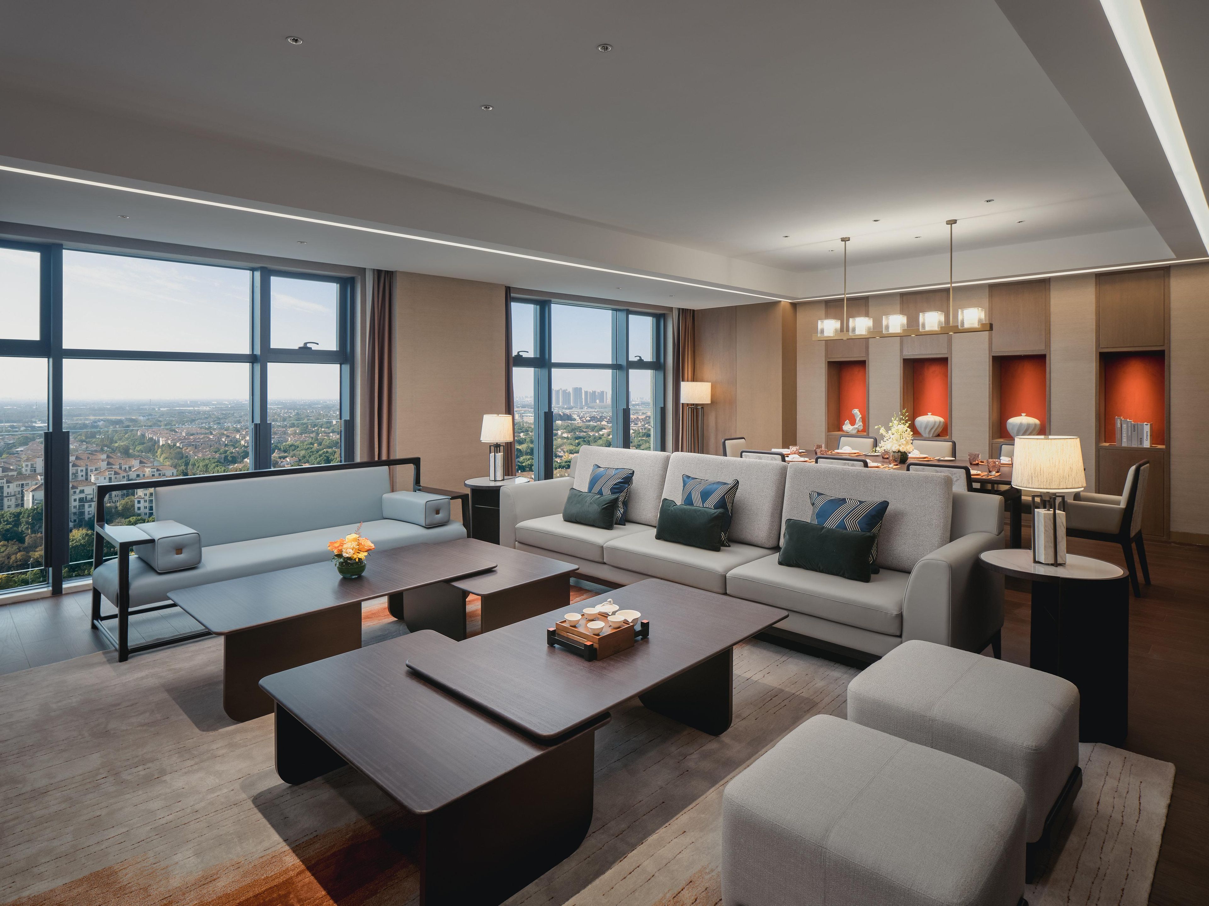 Quarto de hotel moderno com ampla vista da cidade, um conjunto de sofás, área de refeições e espaço bem iluminado.