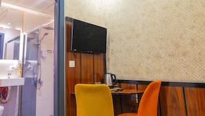 Quarto pequeno e moderno com lambris de madeira, televisão e duas cadeiras.