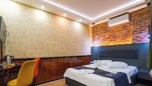 Quarto de hotel com uma cama, uma cadeira de madeira, uma mesa com chaleira e uma parede de tijolos.