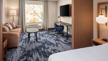 Quarto de hotel com uma cama, uma escrivaninha, uma cadeira, uma televisão e um abajur.