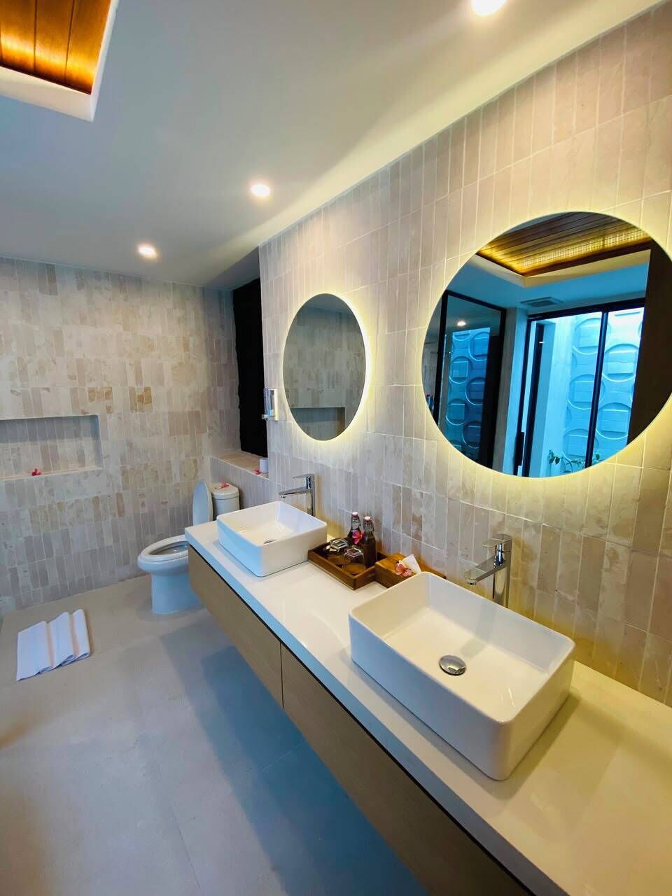 Uma casa de banho moderna com uma toucador comprido, duas pias, uma sanita e um espelho com moldura circular.