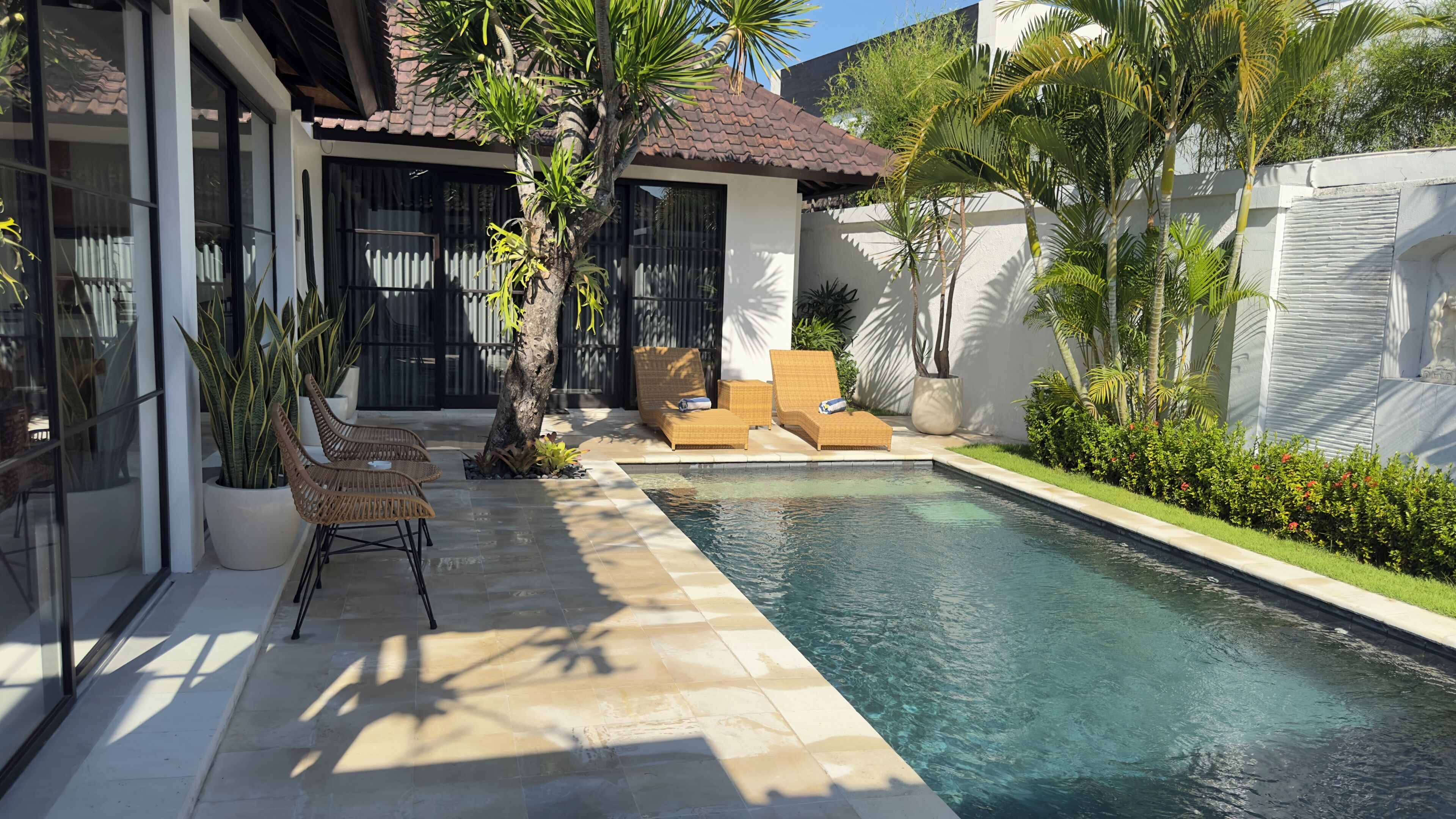 Uma área de piscina com espreguiçadeiras, um vaso de planta e um deck revestido de azulejos.