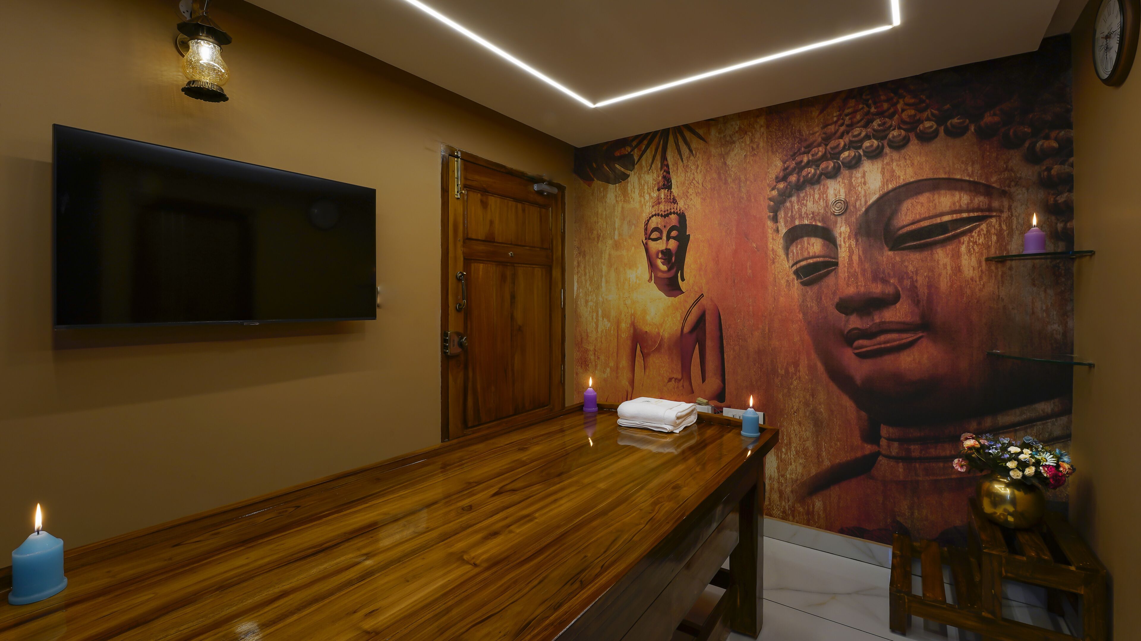 Quarto com um banco de madeira, TV fixada na parede, um mural de Buda e uma vela no chão.