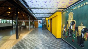 Um corredor com piso xadrez, uma estátua de Buda e um mural de elefantes e uma figura em um trono.