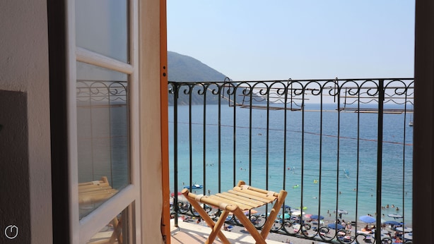 Uma varanda com vista para o mar, uma cadeira de madeira e um corrimão de metal.