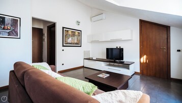 Uma sala de estar moderna com um sofá marrom, uma mesa de centro, uma televisão de tela plana e um armário branco.