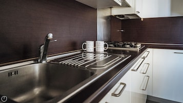 Cozinha moderna com pia de aço inoxidável, duas canecas brancas, fogão a gás e armários brancos.