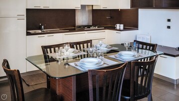 Uma sala de jantar com uma mesa de vidro posta para dois, rodeada por cadeiras de madeira.