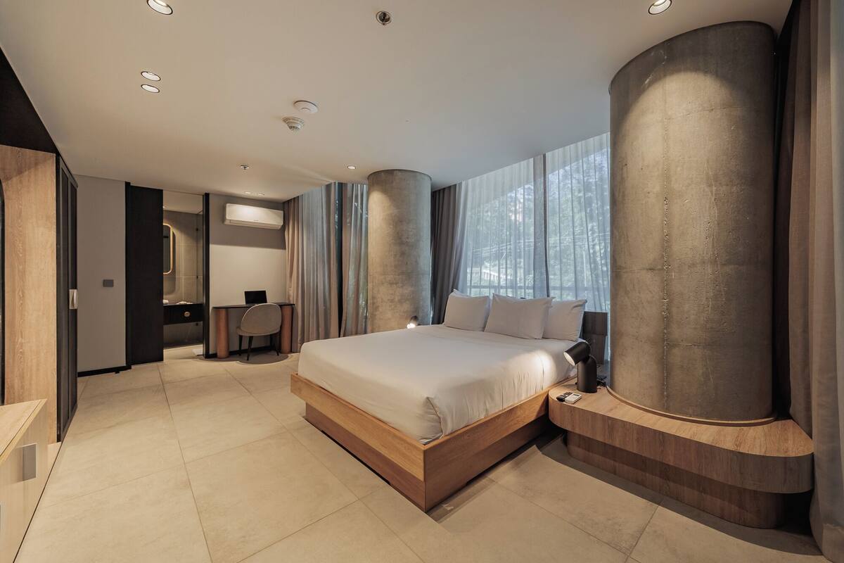 Quarto de hotel moderno com uma cama grande, uma mesa de trabalho e um banheiro.