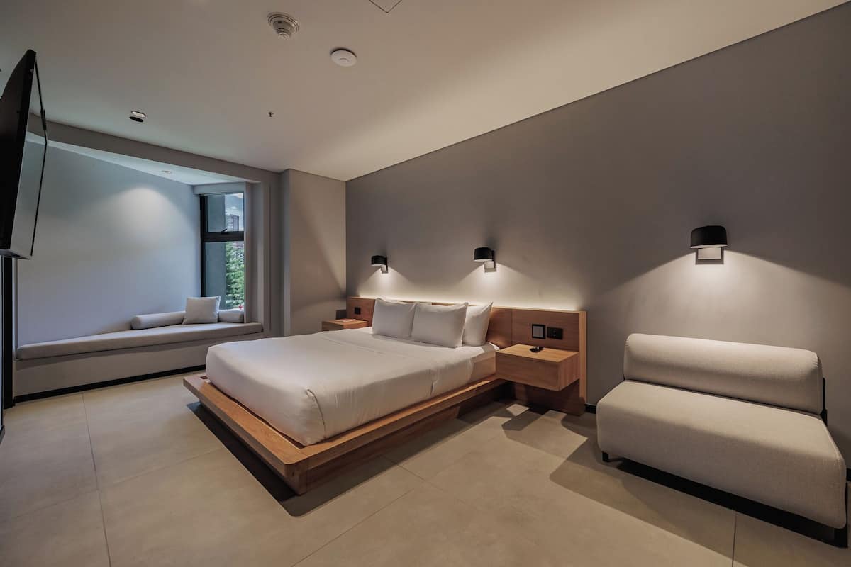 Quarto moderno com cama grande, mesas de cabeceira, uma cadeira e janela com vista.