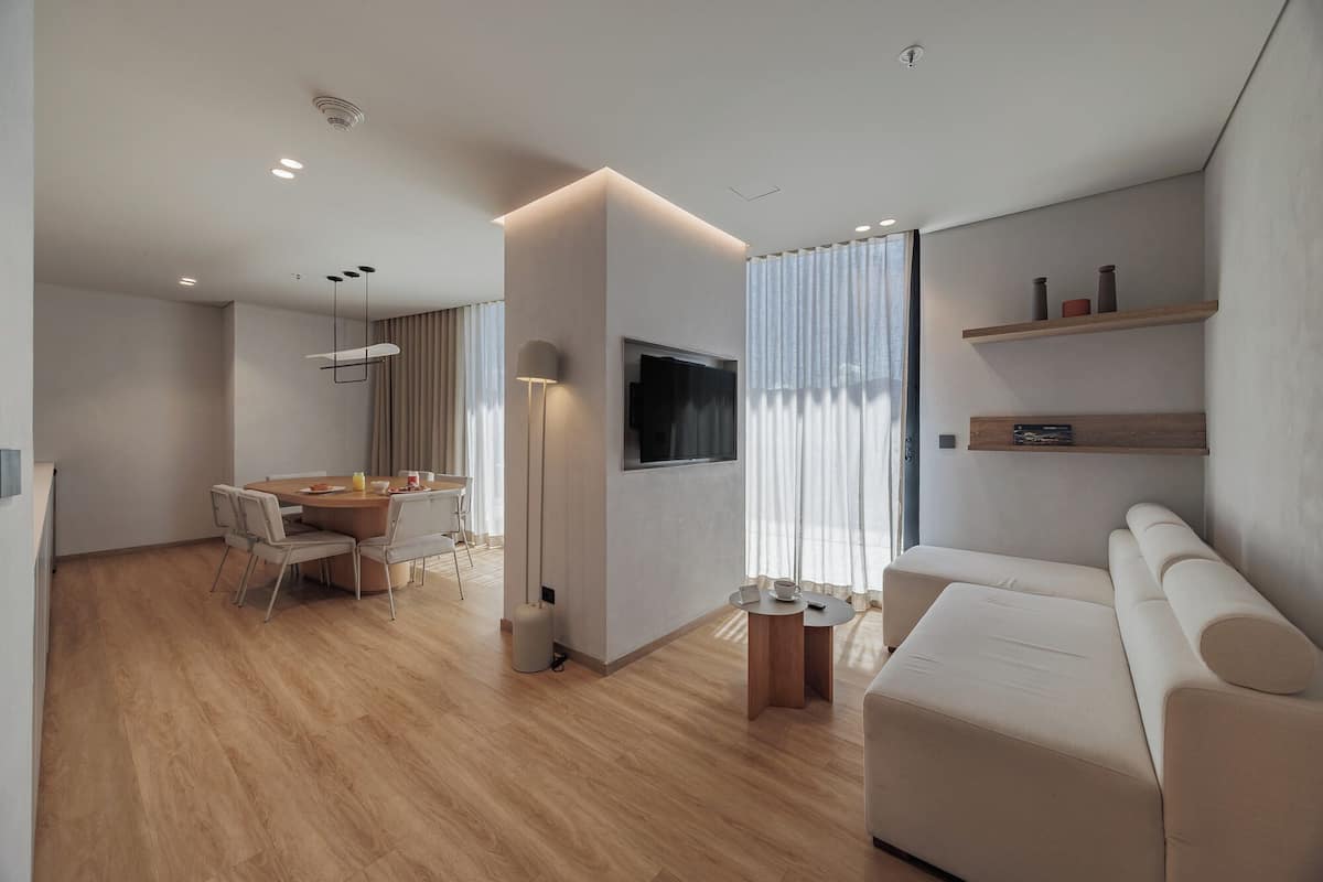 Uma sala de estar moderna com sofá, área de jantar com mesa e cadeiras, e uma TV fixada na parede.