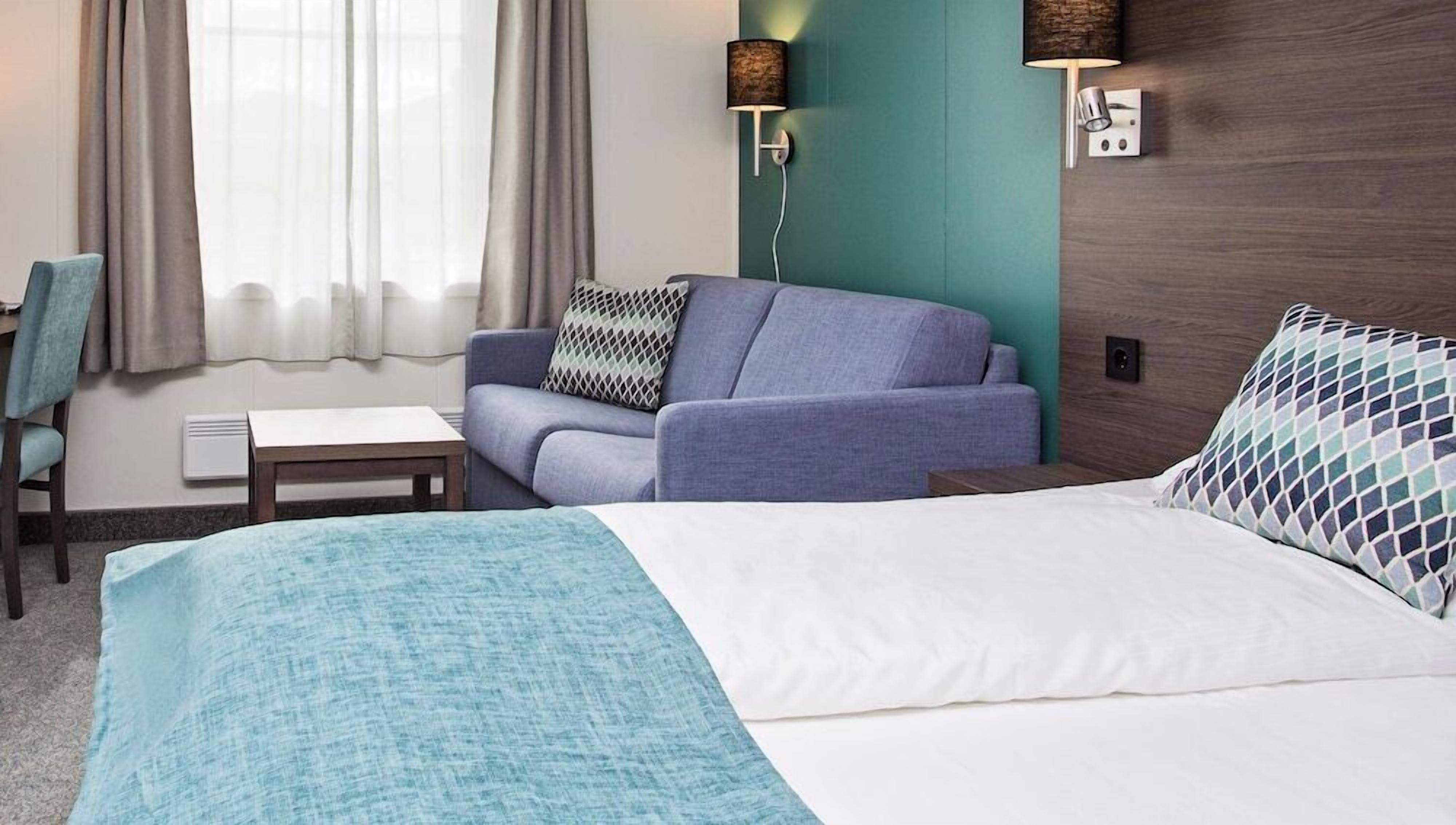 Quarto de hotel com cama, sofá, escrivaninha e cadeira.