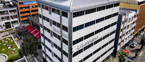 Um edifício moderno com o nome "SOJOURN" em destaque. Apresenta uma grade de janelas e um telhado plano.