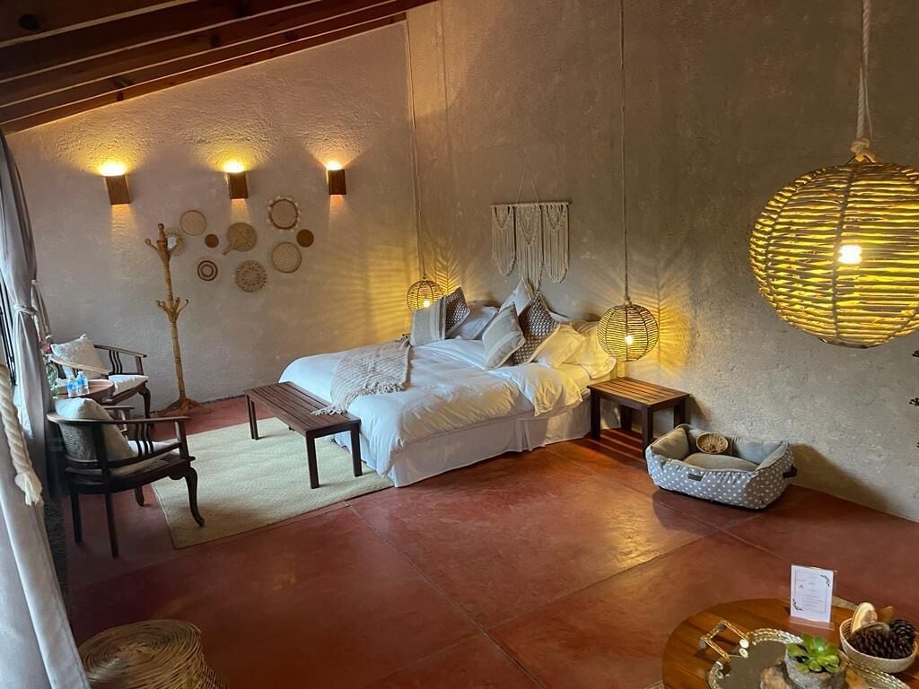 Um quarto aconchegante com cama, mesas de cabeceira, uma poltrona e um lustre.