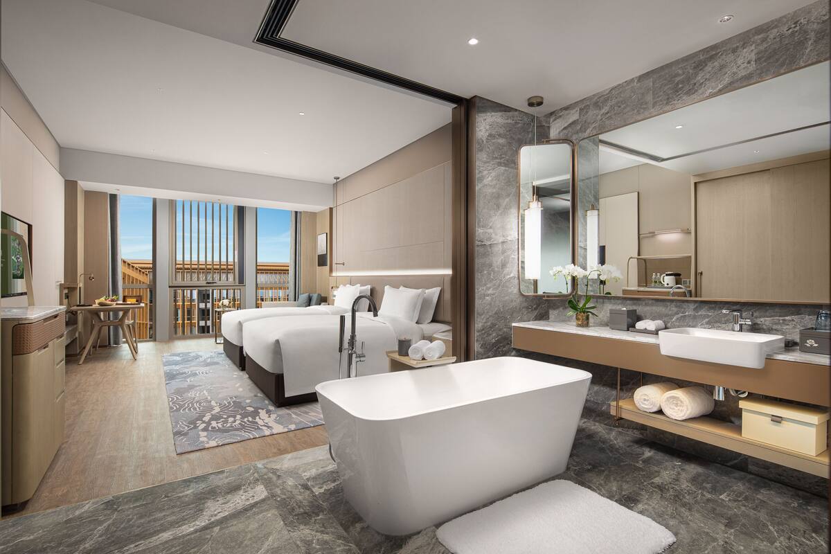 Quarto de hotel moderno com uma banheira grande, quarto separado, varanda com vista e banheiro bem equipado.