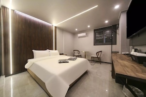 Quarto de hotel moderno com uma cama grande, uma escrivaninha, uma cadeira e uma televisão.