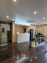 Um hall de hotel moderno com uma mesa de recepção, uma escadaria e um corredor que dá para os quartos.
