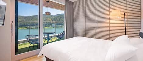 Quarto com cama grande, vista para um lago e varanda com cadeiras.