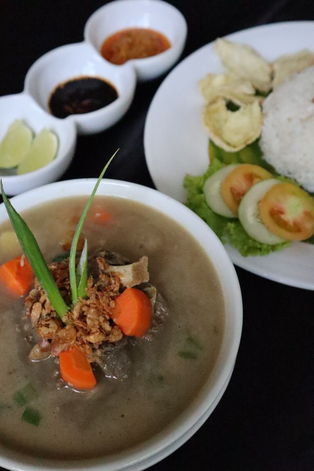 Uma tigela de sopa com legumes e guarnições, um prato de arroz e legumes, e pequenas porções de acompanhamentos.