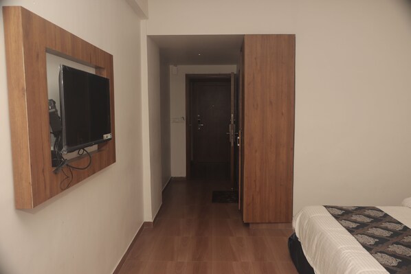 Quarto com guarda-roupa de madeira, cama com colcha estampada e televisão na parede.