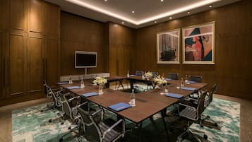 Uma sala de conferências com uma mesa grande, cadeiras, uma TV de tela plana e obras de arte nas paredes.