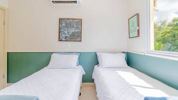 Quarto com duas camas de solteiro, janela com vista para área verde e aparelho de ar condicionado.