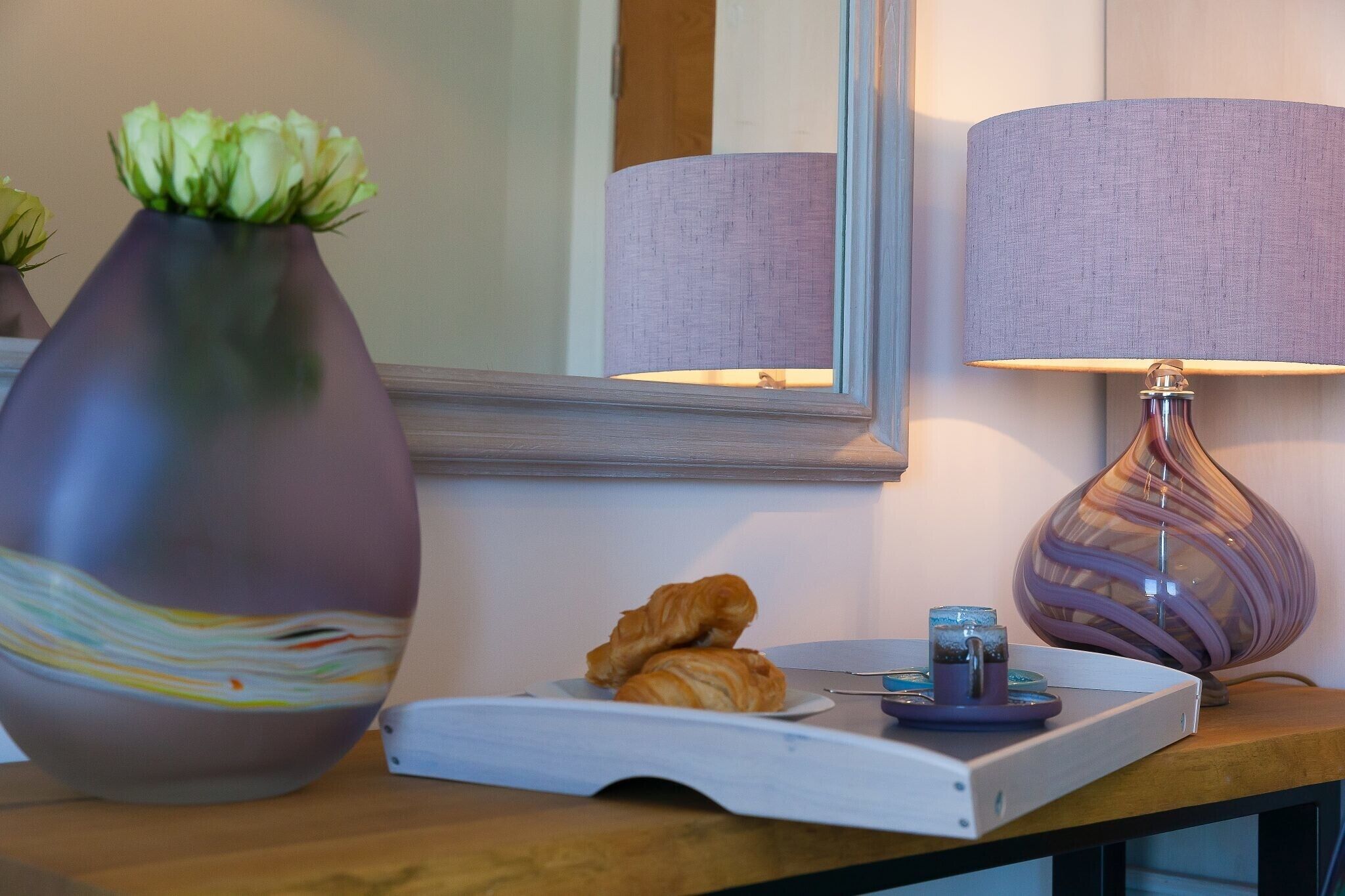 Uma mesa com um vaso, uma lâmpada e um croissant.