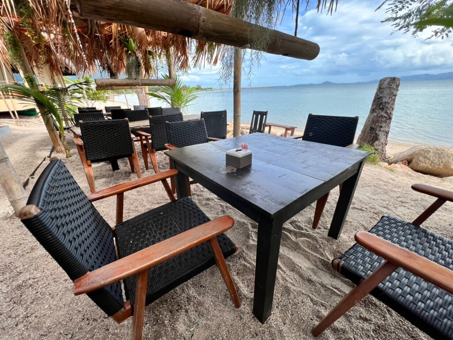 Uma área de estar ao ar livre à beira-mar, com mesa e cadeiras, com vista para um mar calmo.
