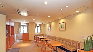 Uma sala de jantar de hotel com mesas e bancos de madeira, uma cozinha compacta e uma janela grande que proporciona luz natural.