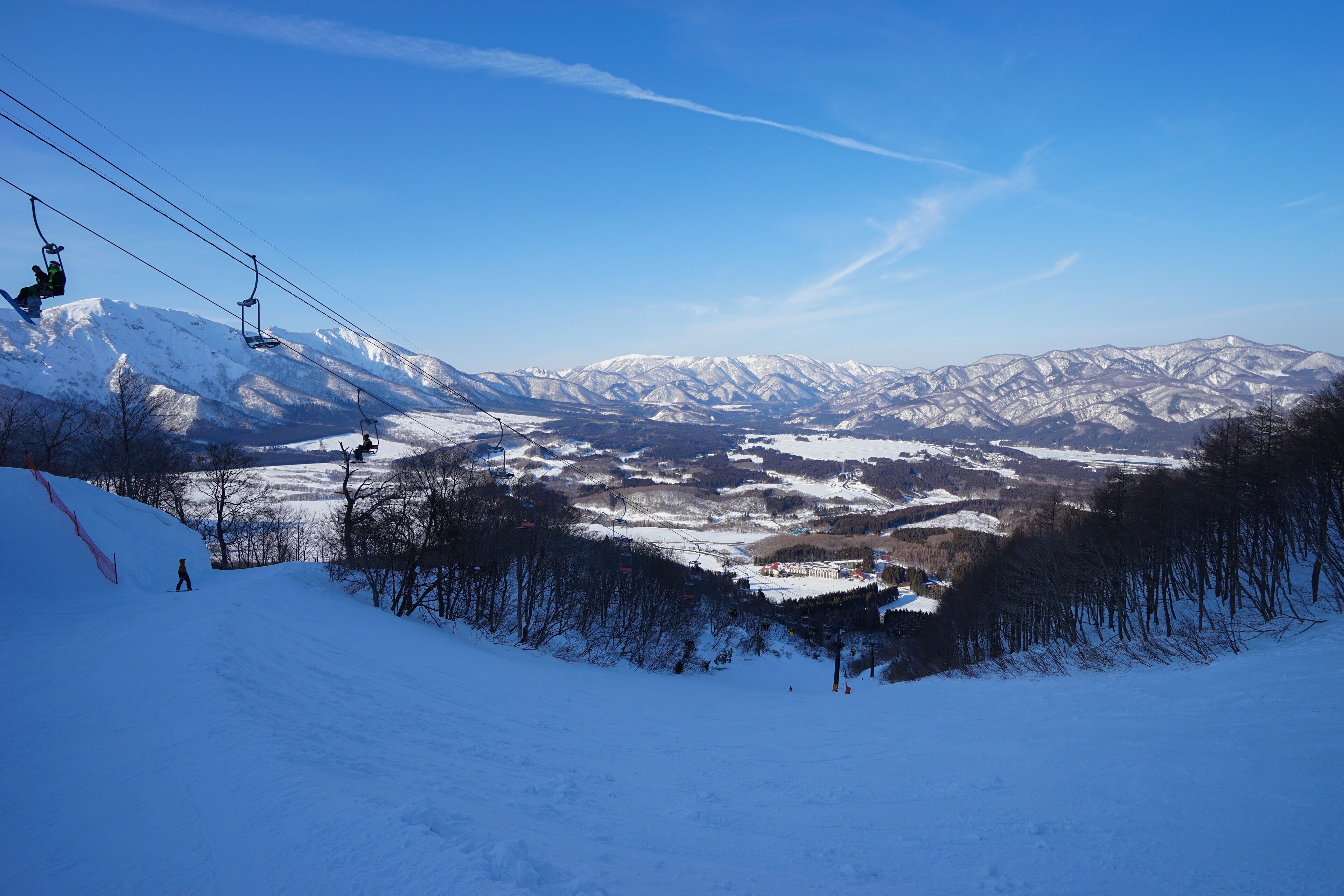 Pista de esqui com teleférico, montanhas cobertas de neve e céu claro.