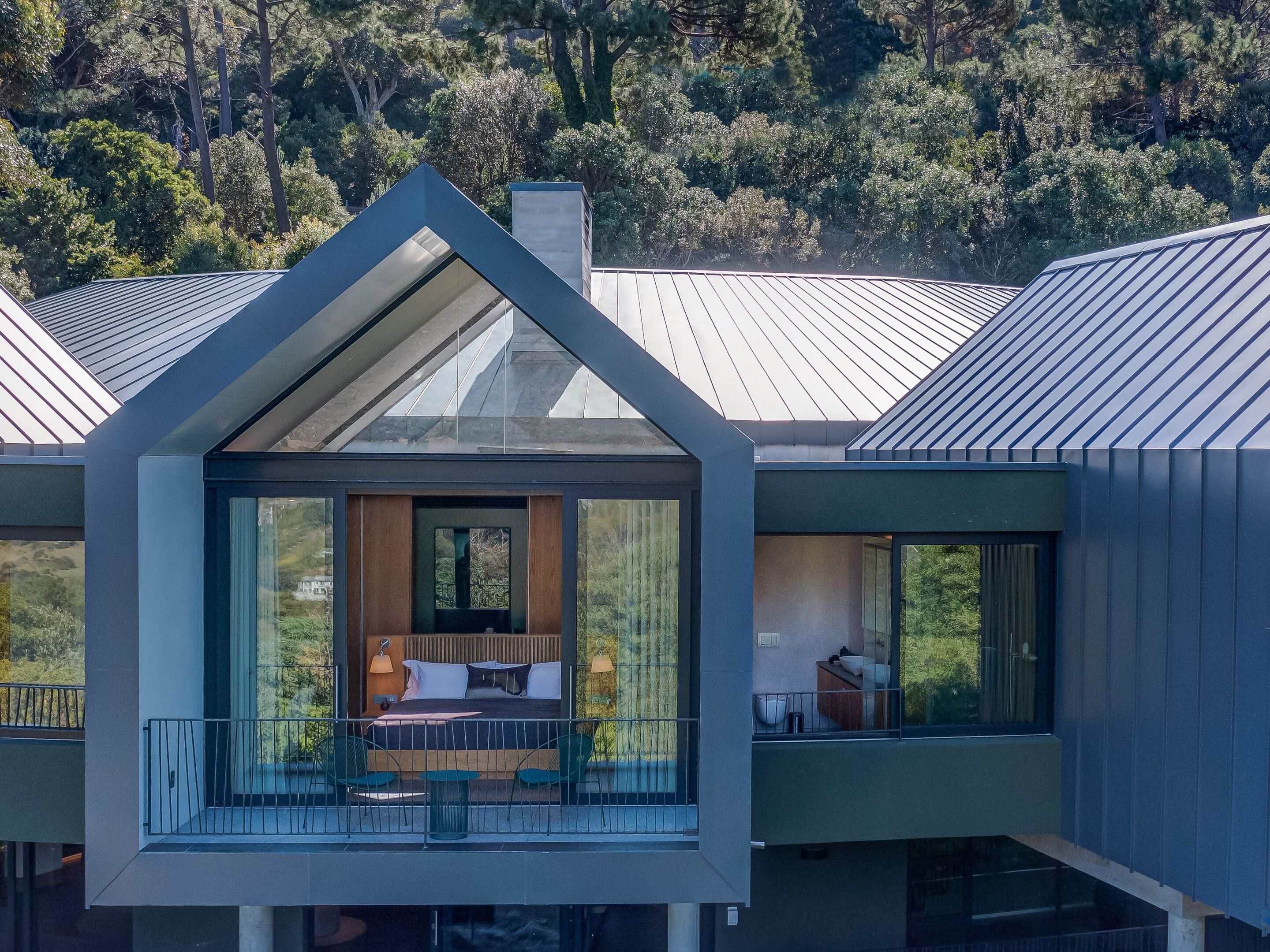 Uma casa moderna com uma varanda grande, um quarto com cama e escrivaninha, e vista para a floresta ao redor.
