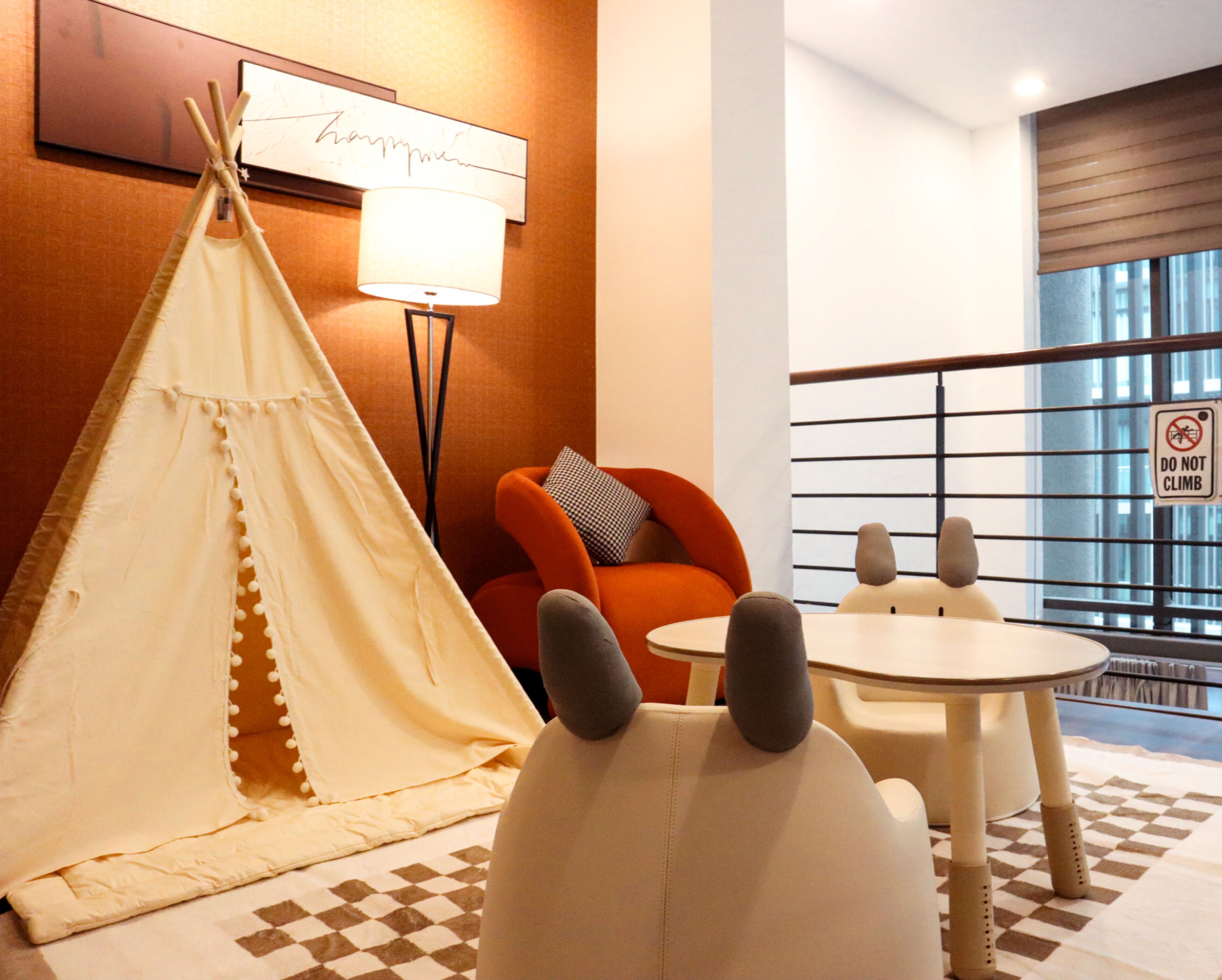 Um quarto com um tipi branco, uma cadeira vermelha e uma mesa com almofadas em formato de animais.