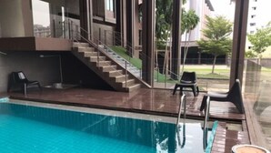 Uma piscina com deck de madeira, escadas e cadeiras ao ar livre.
