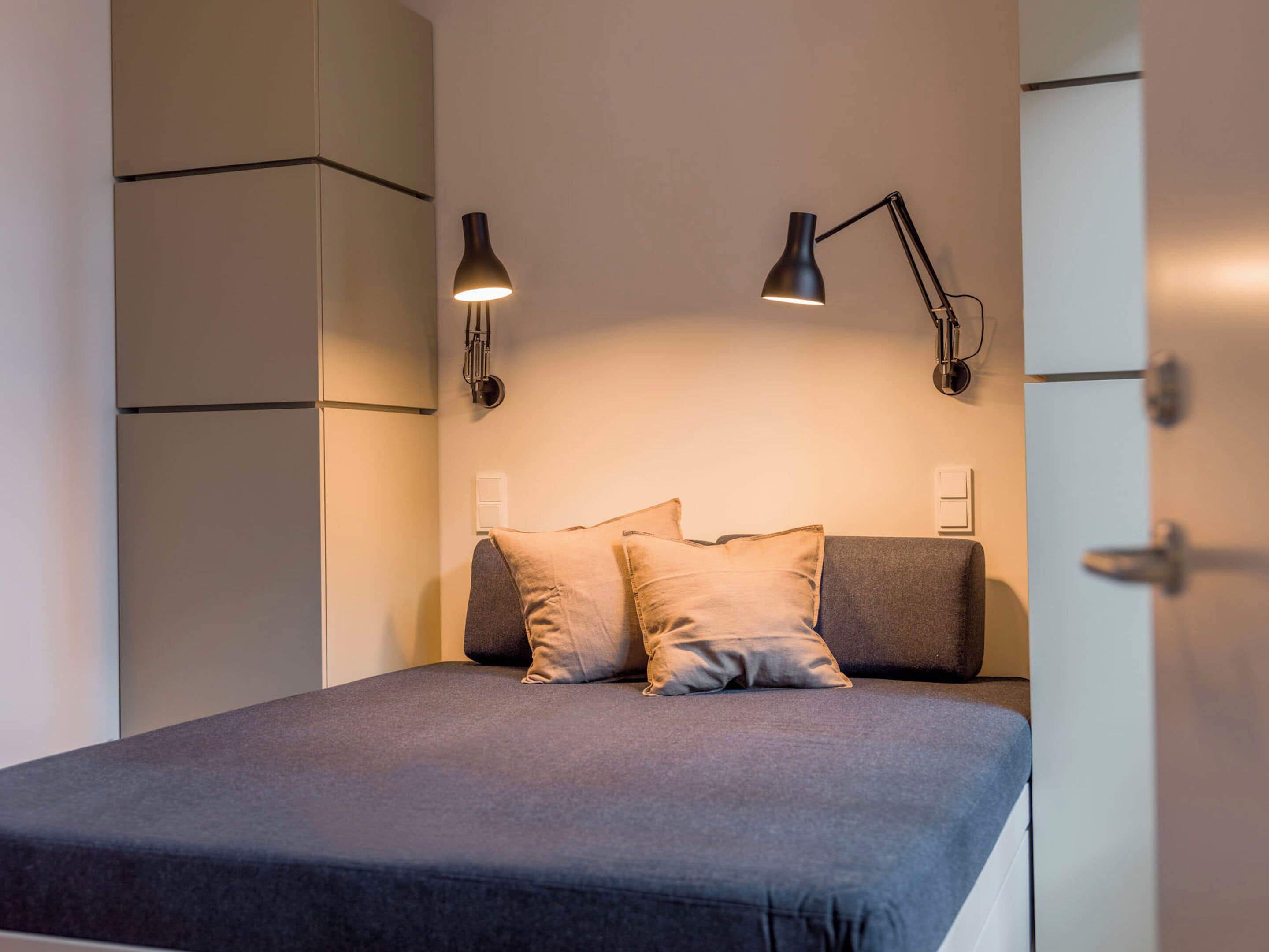 Quarto com cama, duas luminárias na parede e um guarda-roupa.
