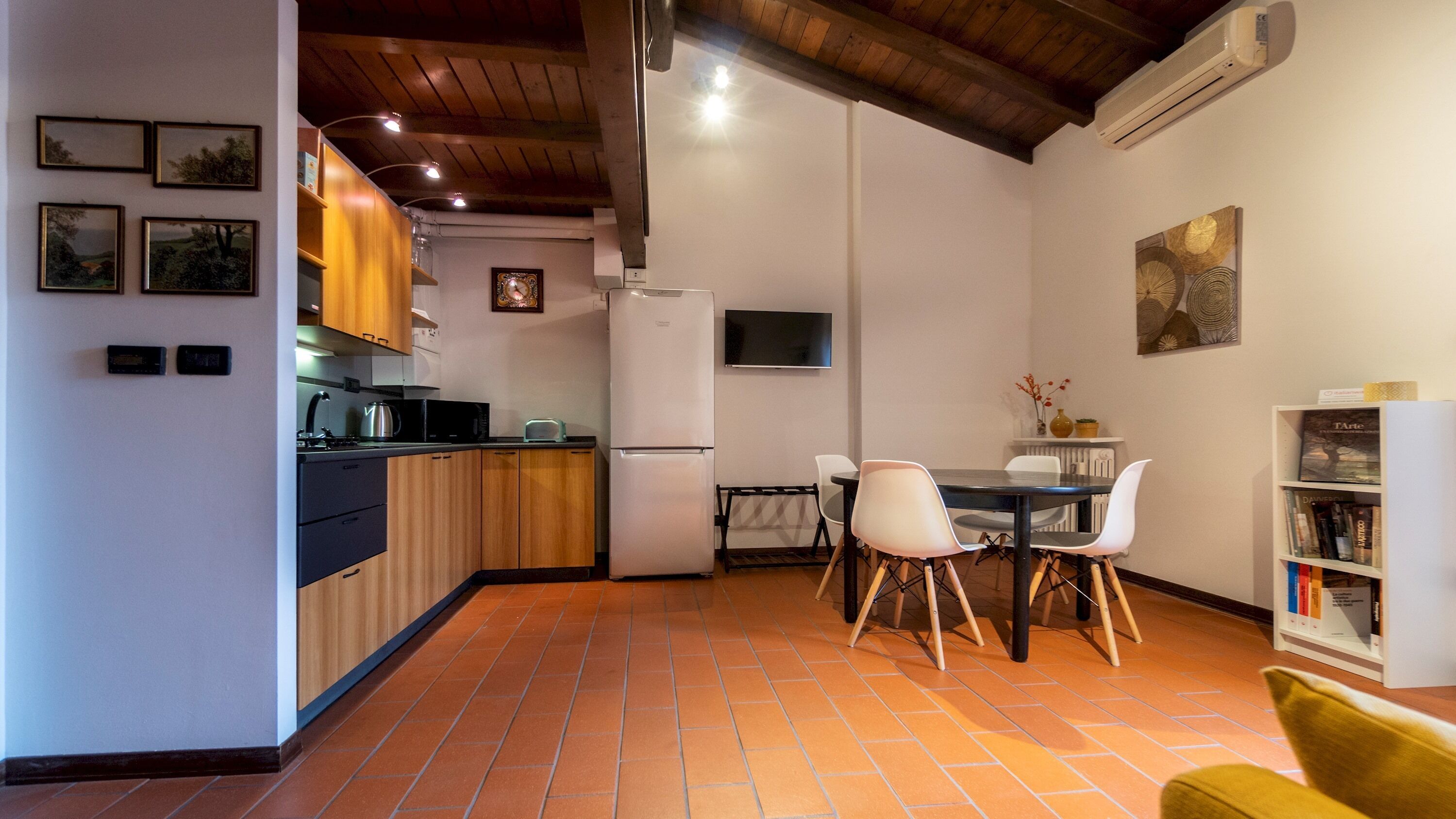 Uma cozinha compacta com armários de madeira, geladeira, mesa de jantar com cadeiras e uma estante.