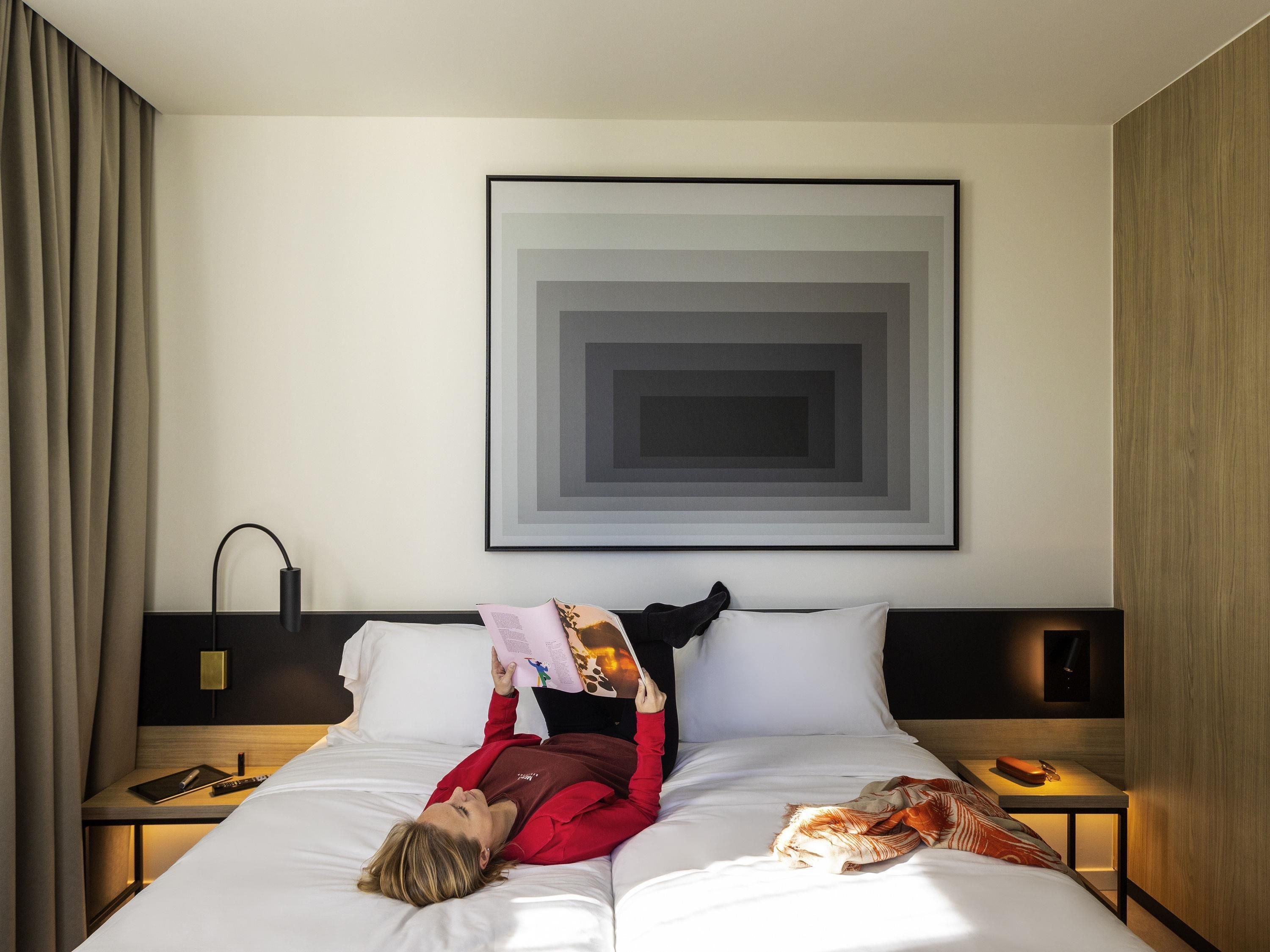 Quarto de hotel com cama, luminária, mesa de cabeceira e uma obra de arte emoldurada na parede.