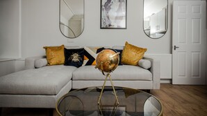 Uma sala de estar moderna com um sofá modular cinza, dois espelhos redondos, um globo em um tripé e uma pintura abstrata emoldurada na parede.