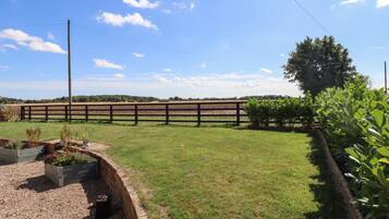 Uma área externa cercada, com um caminho de cascalho, cerca de madeira e um gramado.