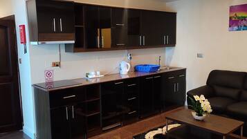 Um espaço compacto com cozinha compacta, sofá e uma pequena mesa com um vaso de flores.