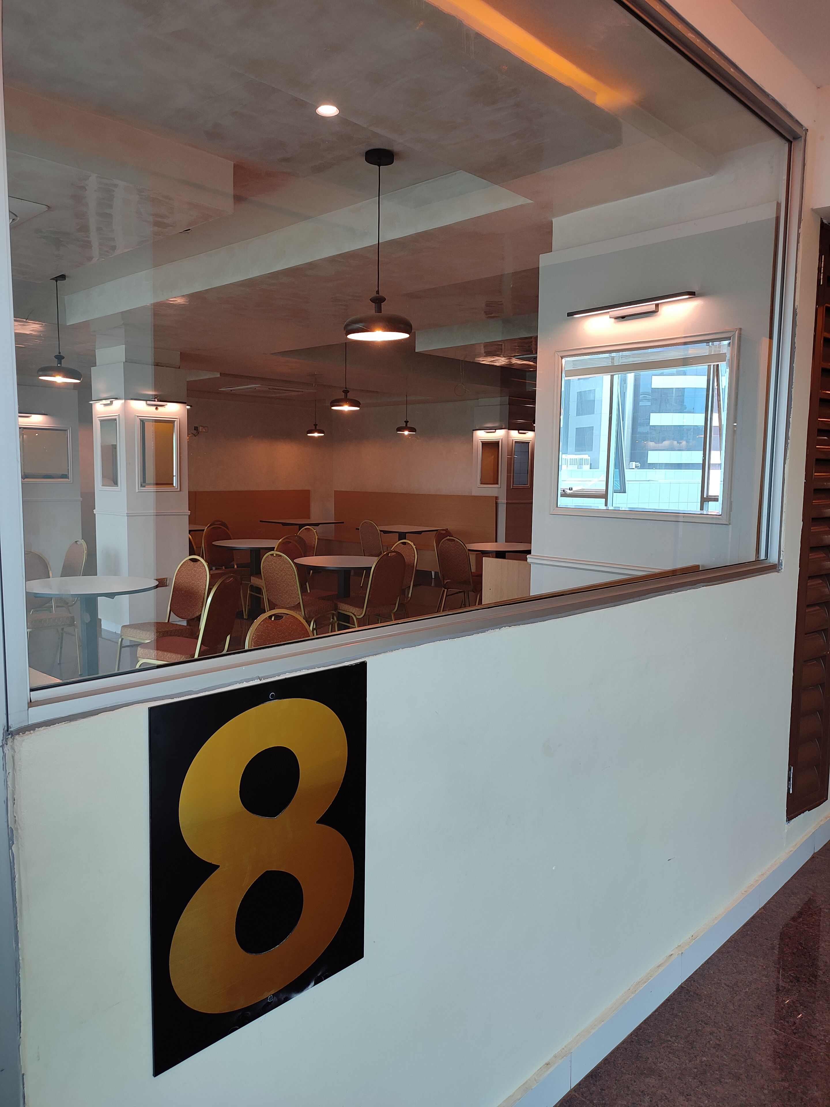Sala de conferências com placa grande com o número 8, mesas, cadeiras e iluminação pendente.
