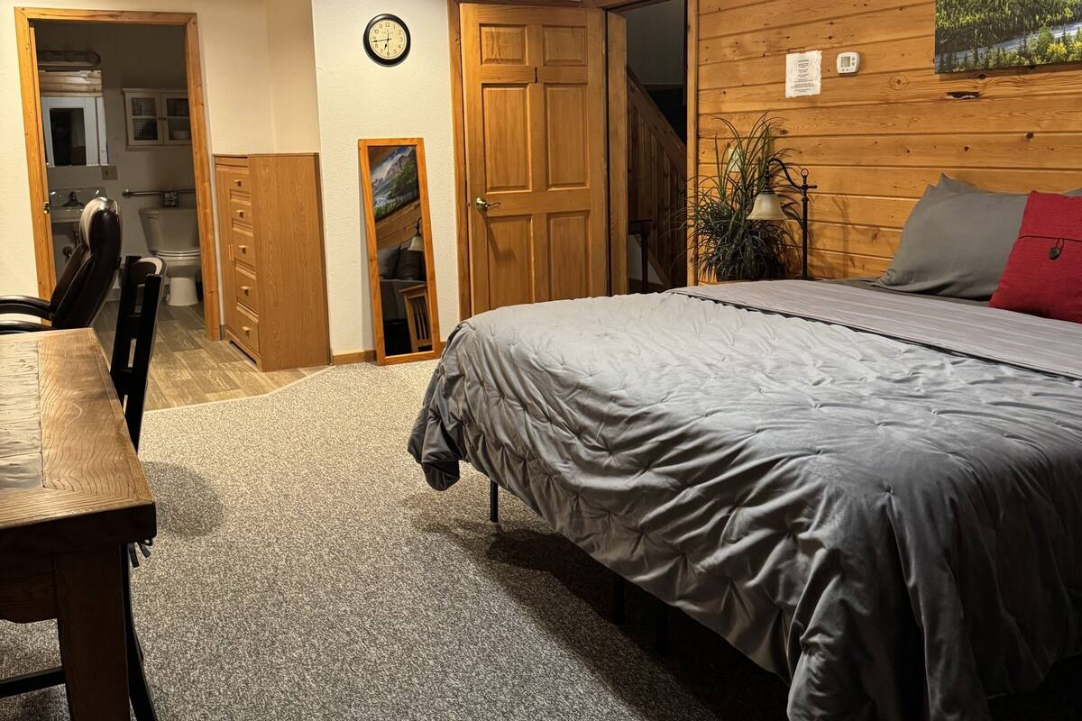 Um quarto com uma cama, uma porta de madeira, um relógio e um quadro na parede.