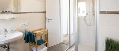 Uma casa de banho moderna com cabine de duche em vidro, uma pia, um espelho e um porta-toalhas.